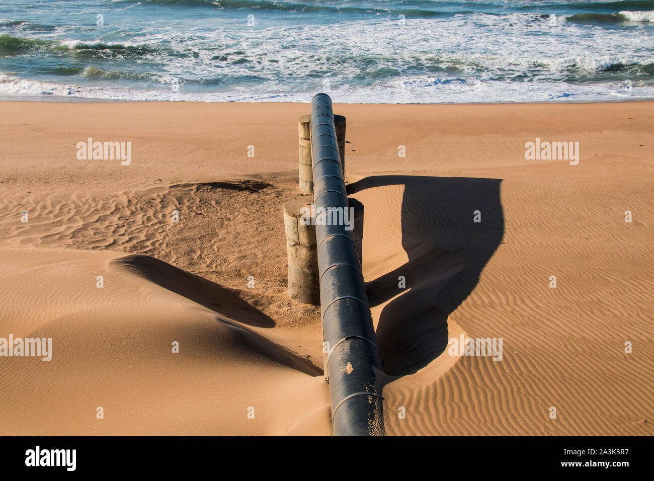 Exposed long black pipe leading into sea at low tide on coastline Stock ...
