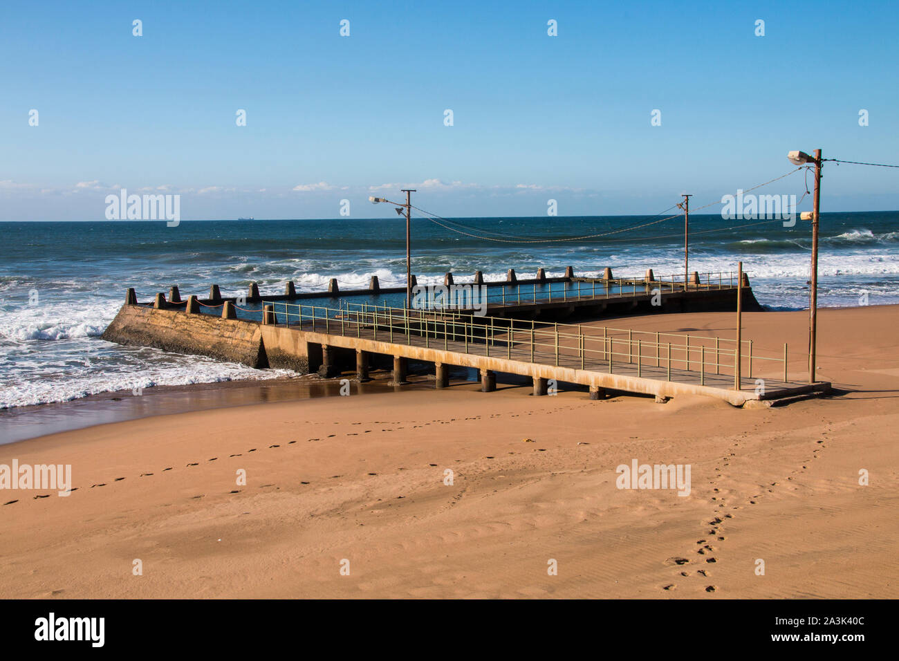 Footprings in beach sand leadinng to concrete tidal pool at low tide ...