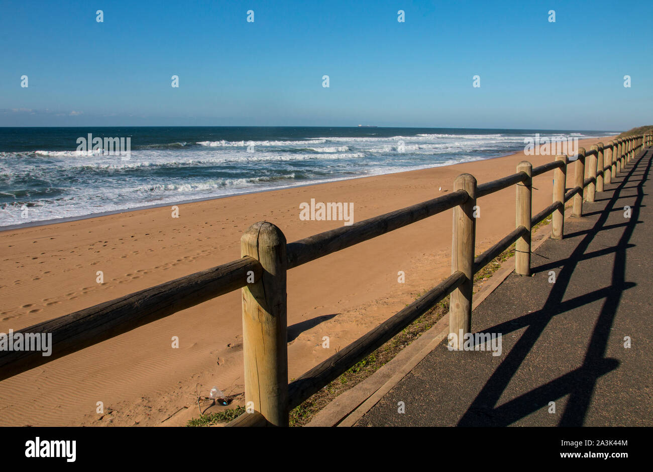 Wooden railing bordering bitumen pathway alongside beach shoreline ...