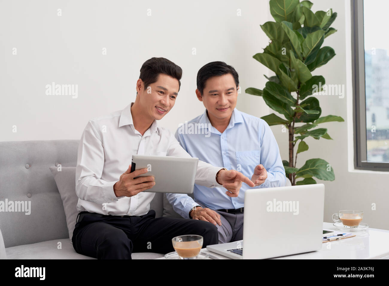 two young men working with laptop and tablet sitting on couch Stock ...