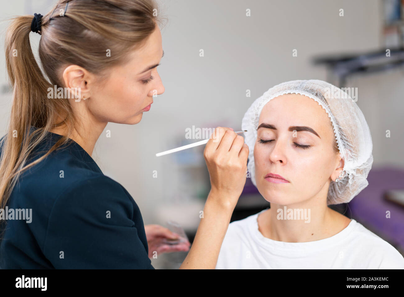 Cosmetology cabinet client sitting on couch. Beautician applies marking ...