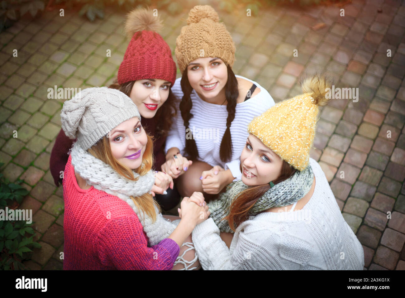 Girls in warm knitted clothes and hats hug, top view. Autumn day, a ...