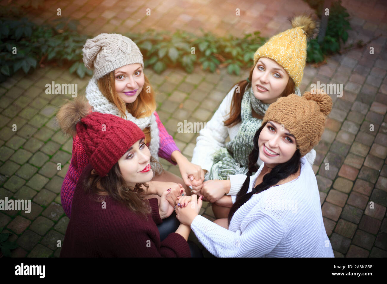 Girls in warm knitted clothes and hats hug, top view. Autumn day, a ...