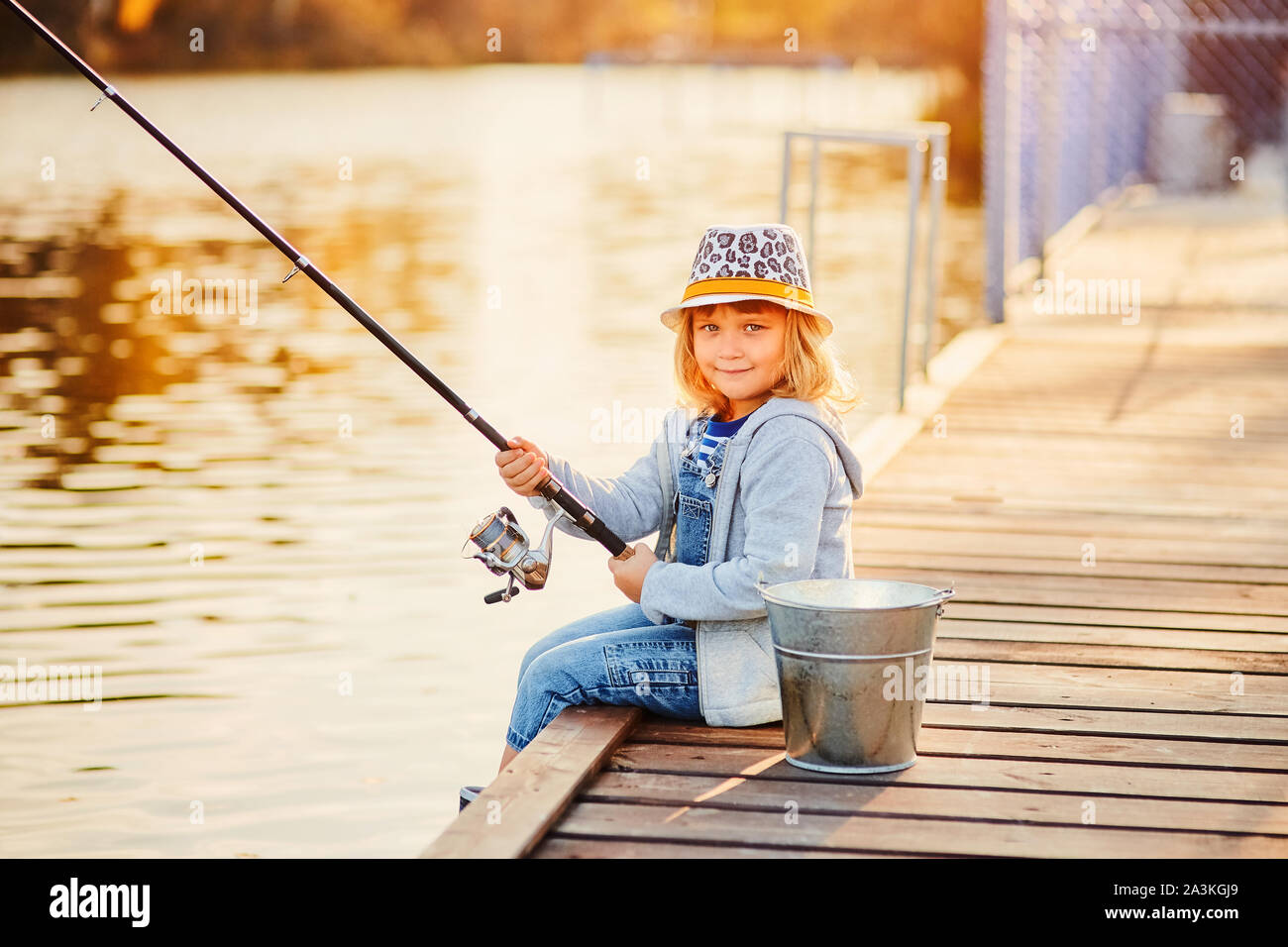 A little girl fishing with a fishing rod from a pontoon or pier on the ...