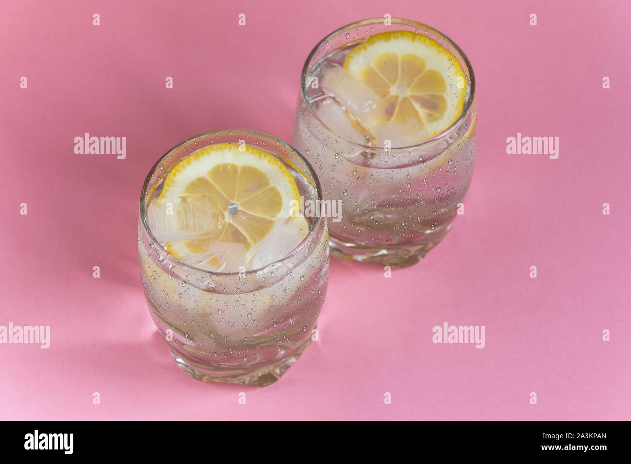 Two glasses of fresh cold water with lemon slices and ice on pastel ...