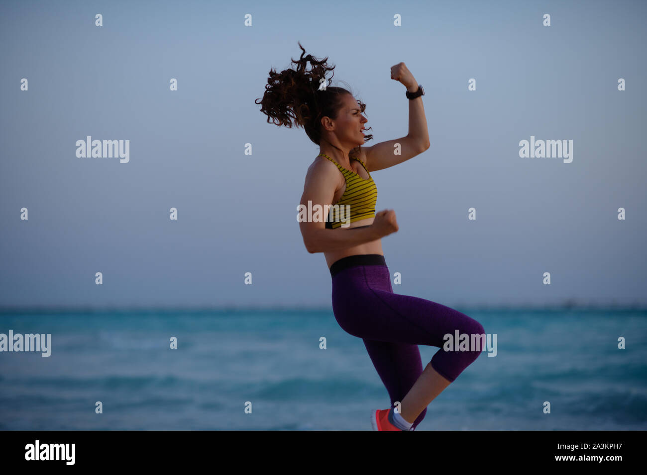 fit woman in fitness clothes on the ocean shore in the evening doing ...