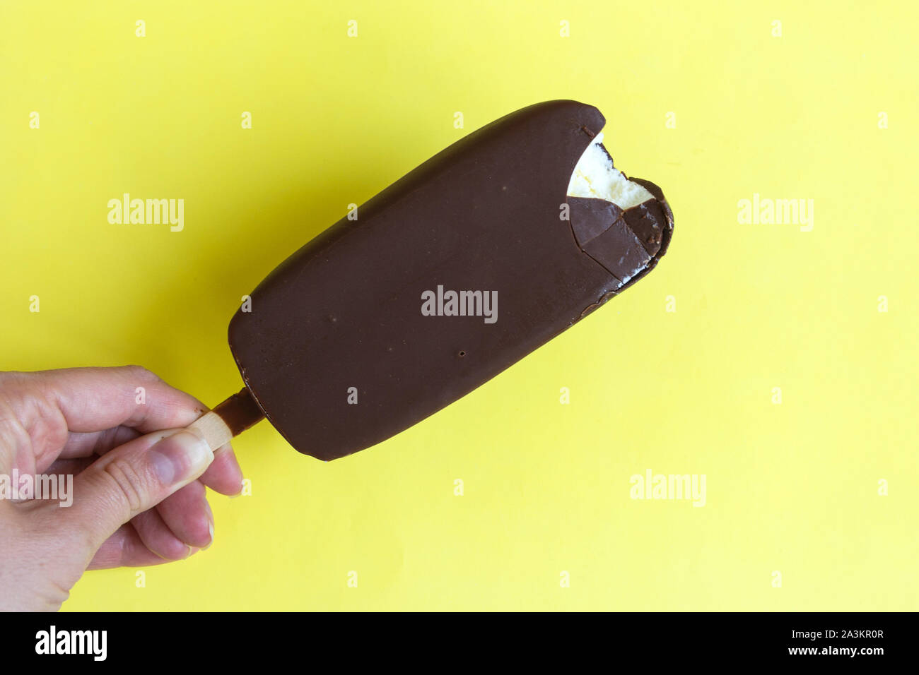 Woman fingers holding bite ice cream in chocolate on pastel yellow ...
