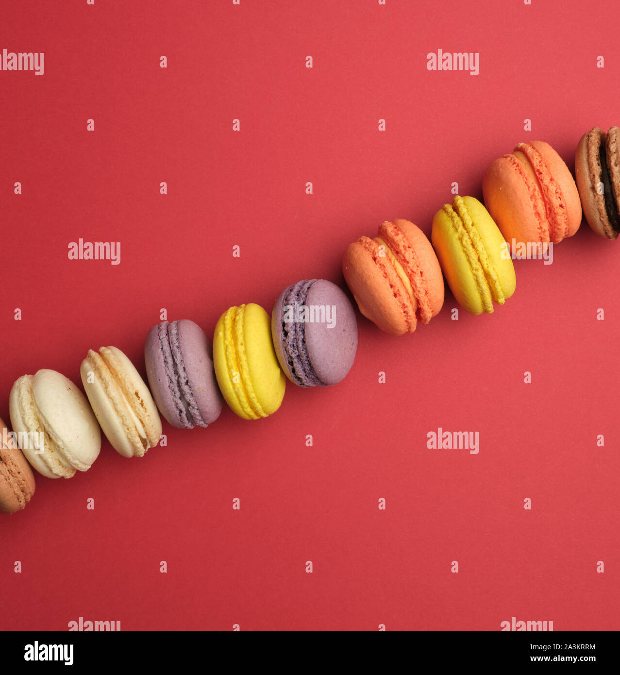 round multi-colored baked macarons with cream lie in a line on a red ...