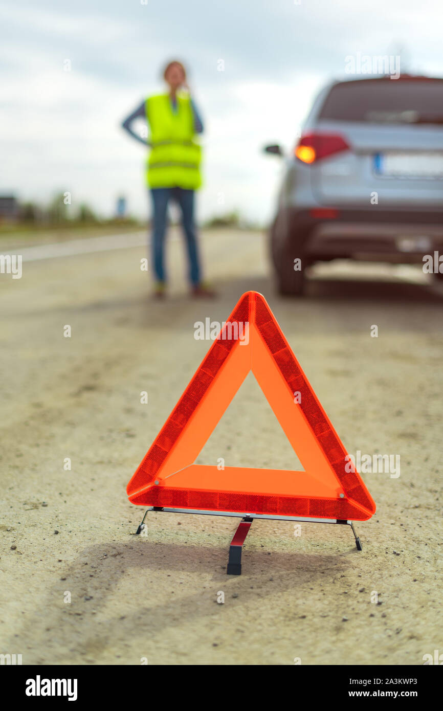 Vehicle breakdown and warning triangle on the road, woman using phone ...