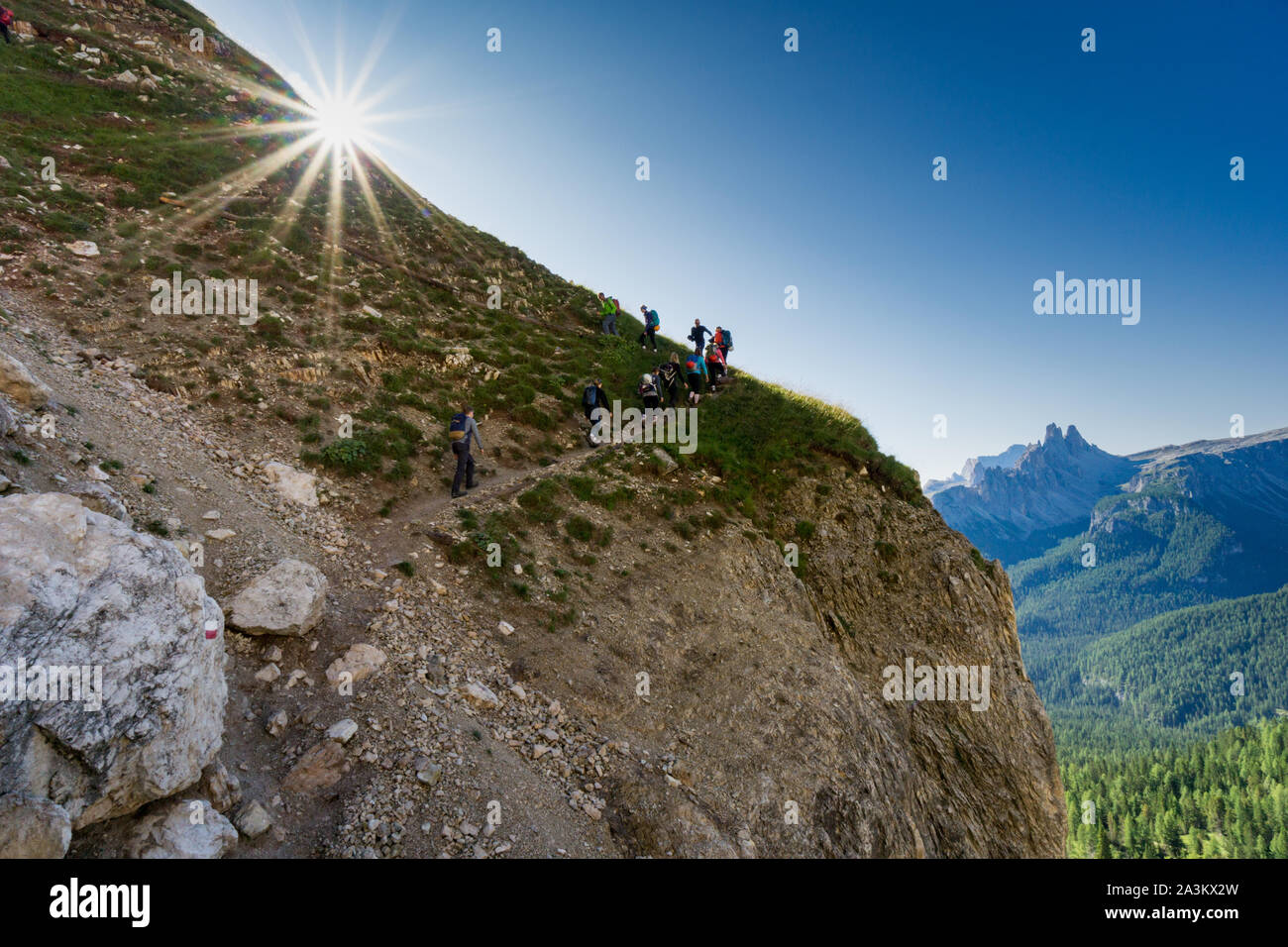 large group of young hikers going up a steep hiking trail with the sun ...