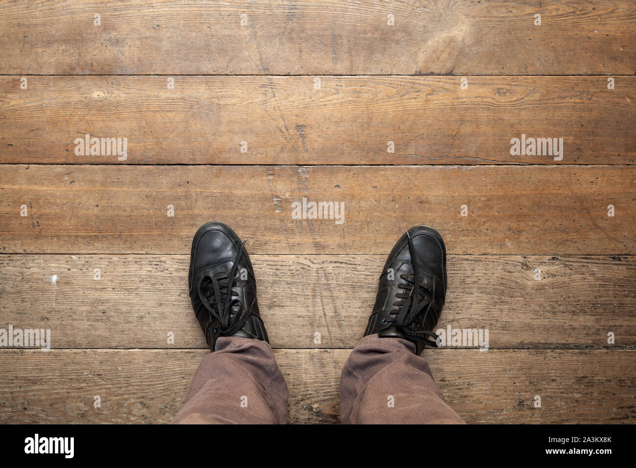 Male feet in shiny black leather shoes stand on grungy wooden floor ...
