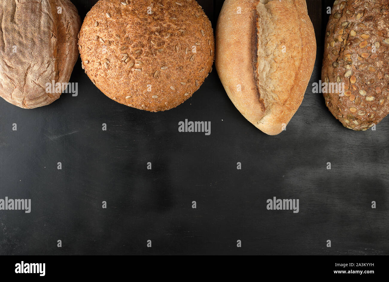 baked various loaves of bread on a black background, empty space, top ...