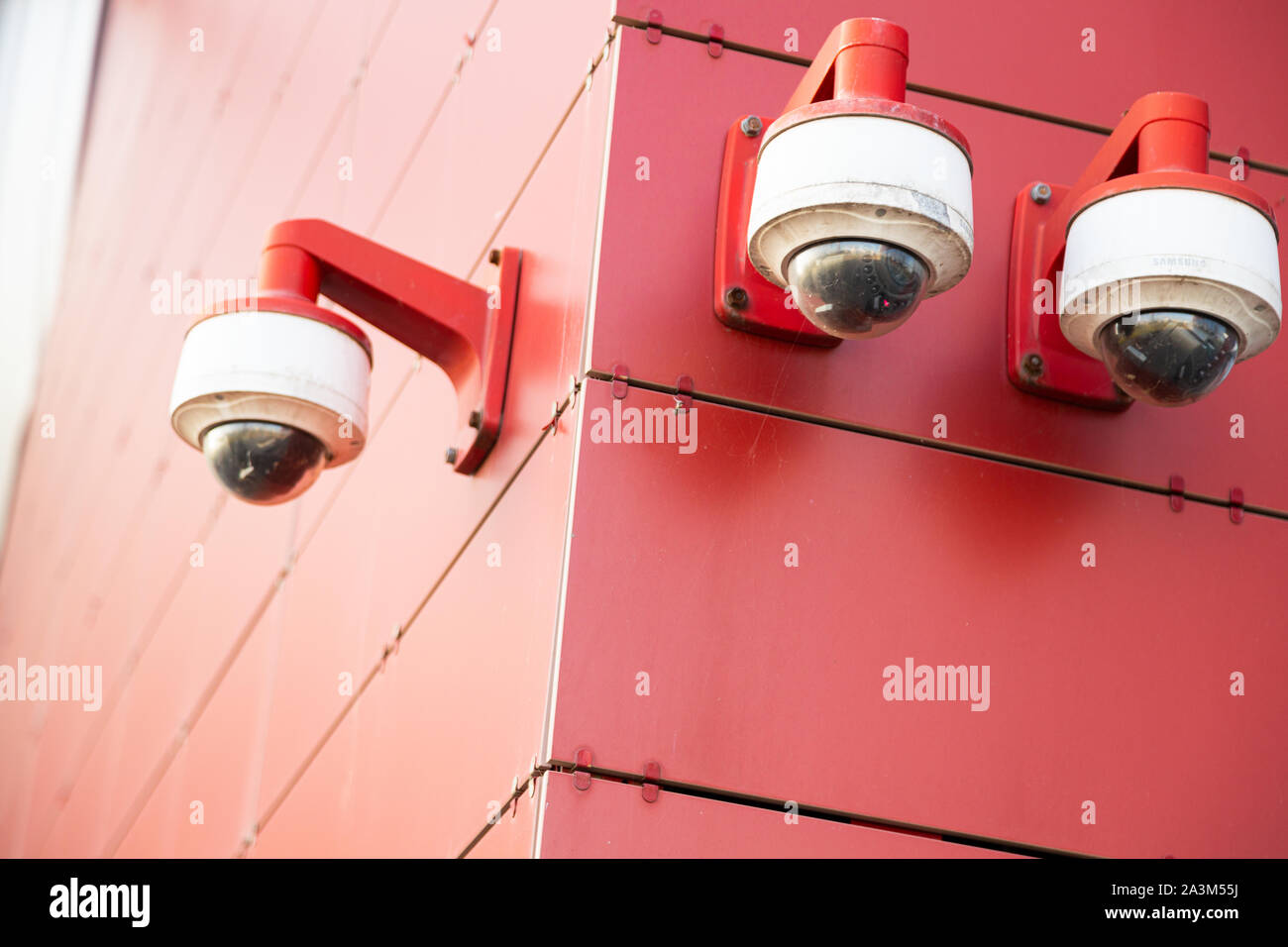 Three red-white surveillance cameras on red metal wall Stock Photo - Alamy