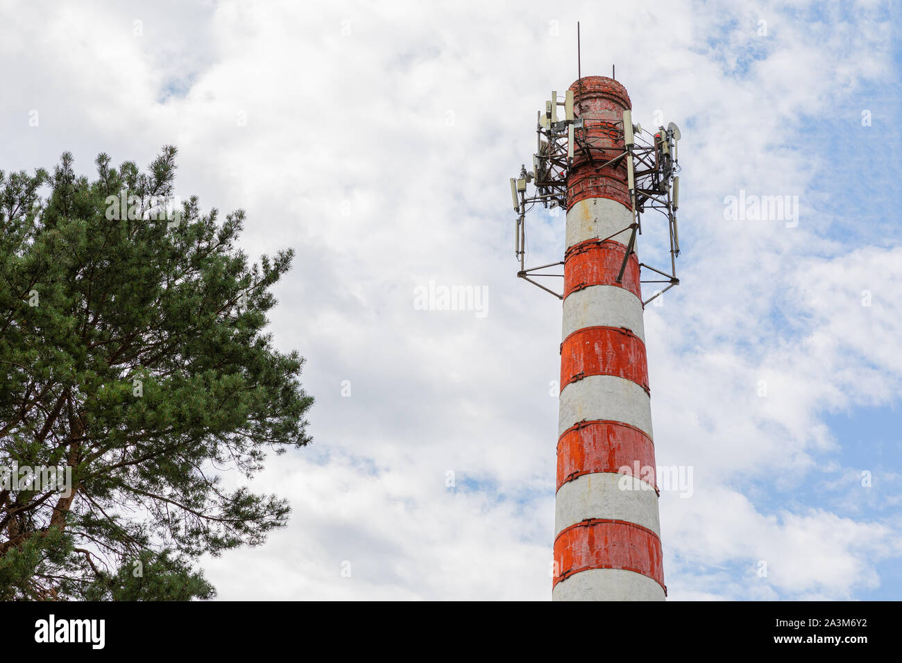 Red white chimney with steel installation on top with tree in blue sky ...