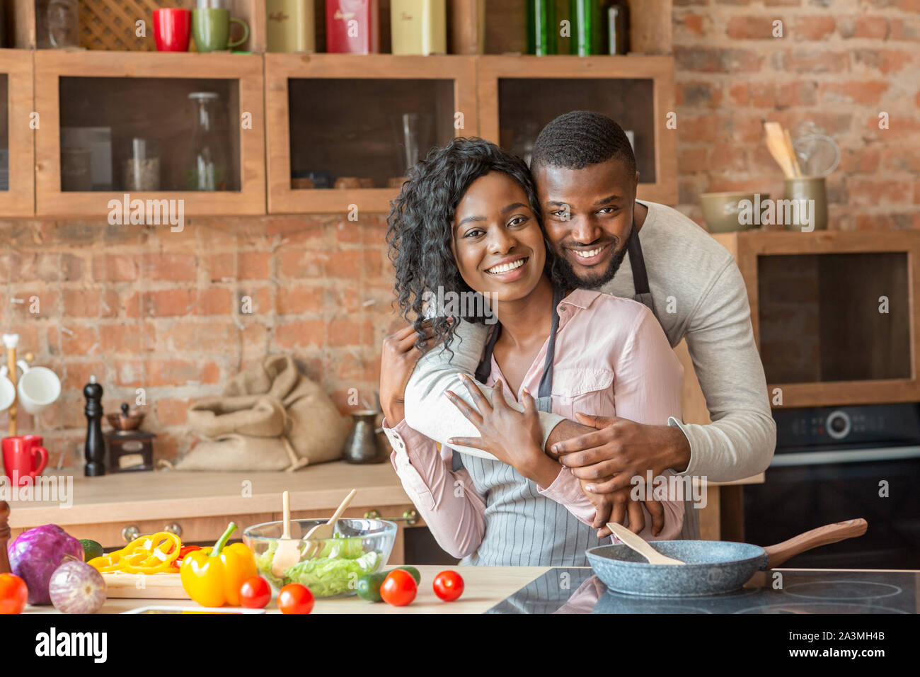 Cheerful black man hugging his wife while cooking at kitchen Stock ...