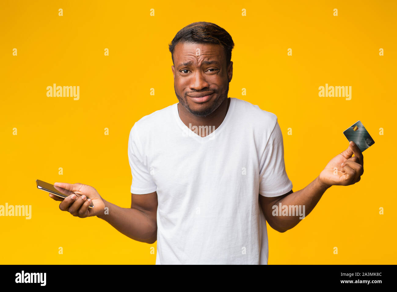 Confused Man Holding Phone And Credit Card Over Yellow Background Stock ...
