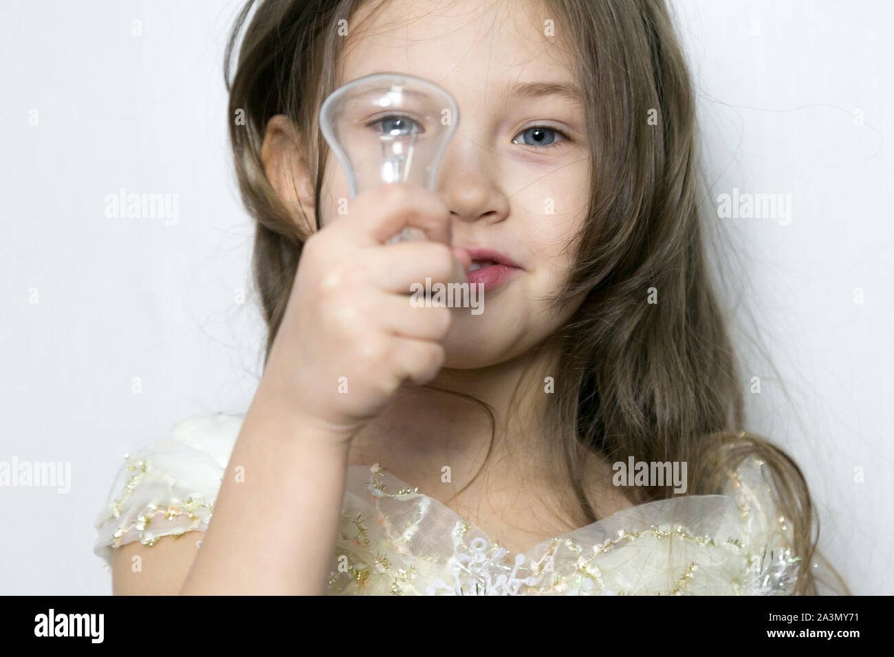 A little girl holds an incandescent lamp her hand and looks through it ...