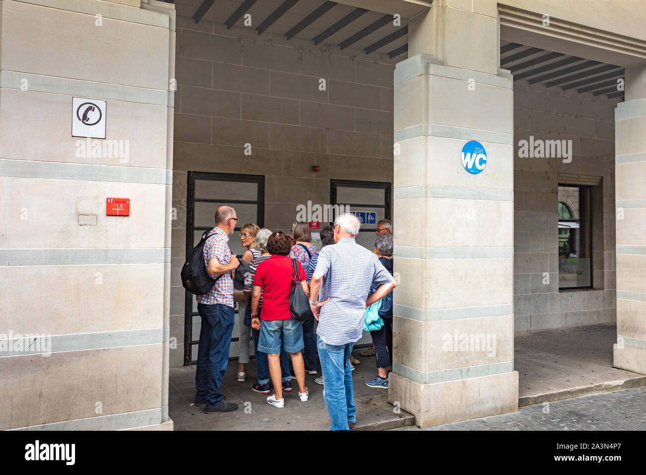 A group of people waiting outside at the entrance of a public toilet in ...