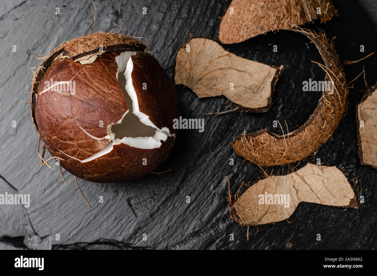 Broken raw coconut on black slate stone background. Diet and vegetarian ...