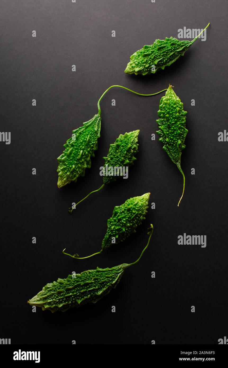 A small green bitter melon or momordica on black background. Flat lay ...