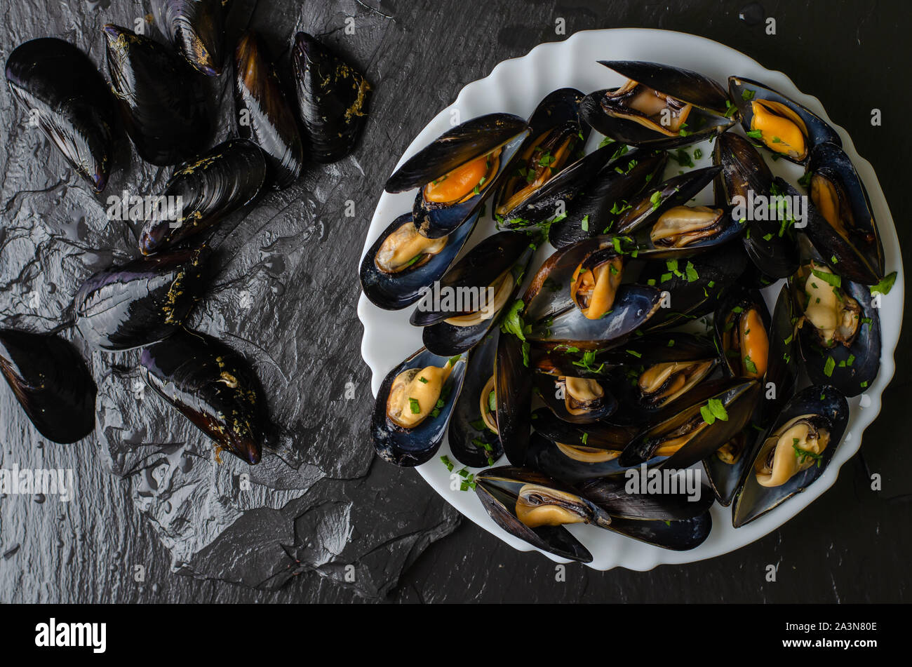Fresh raw and cooked mussels on black slate stone background. Seafood ...