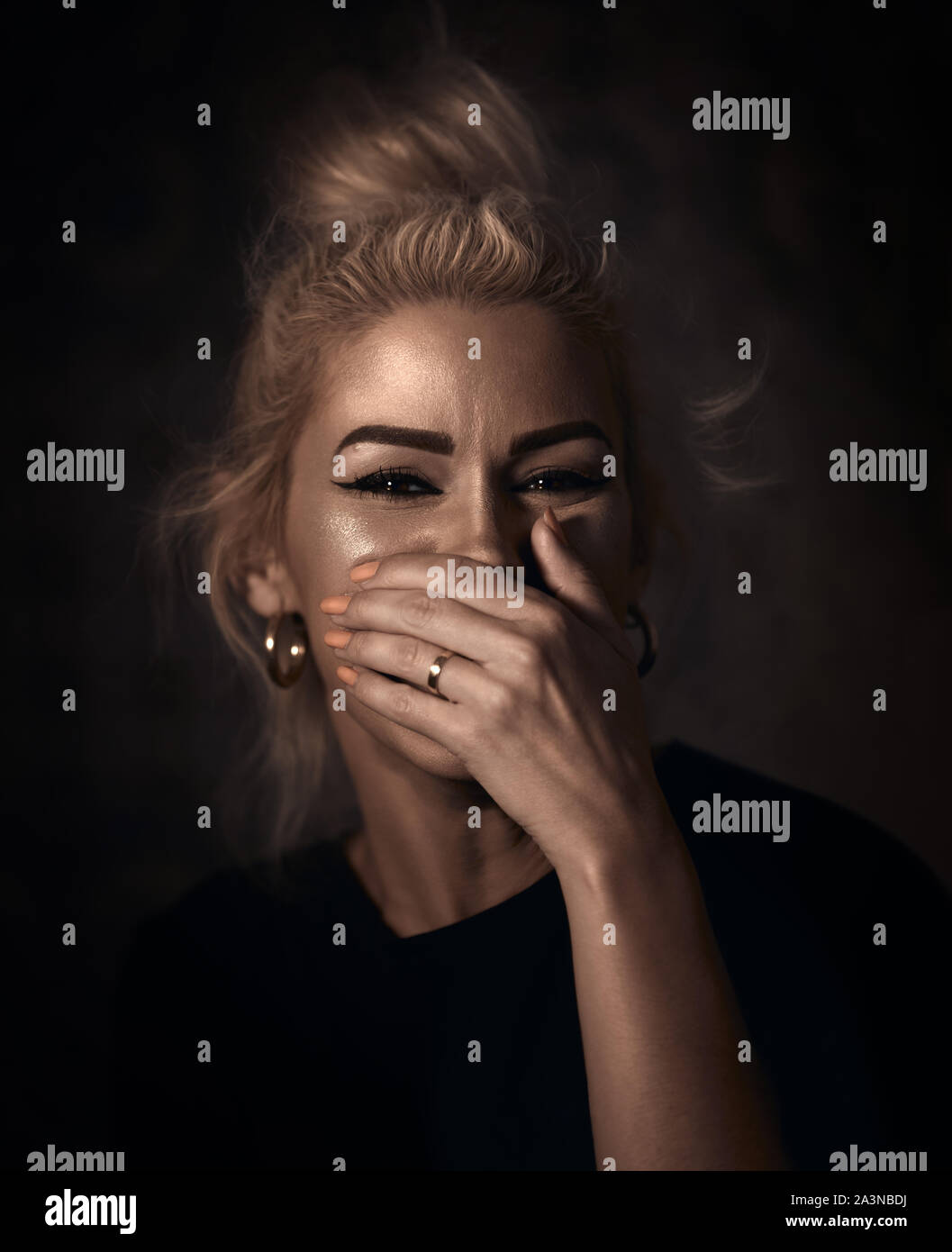 Portrait of a blonde woman hiding her laugh Stock Photo - Alamy