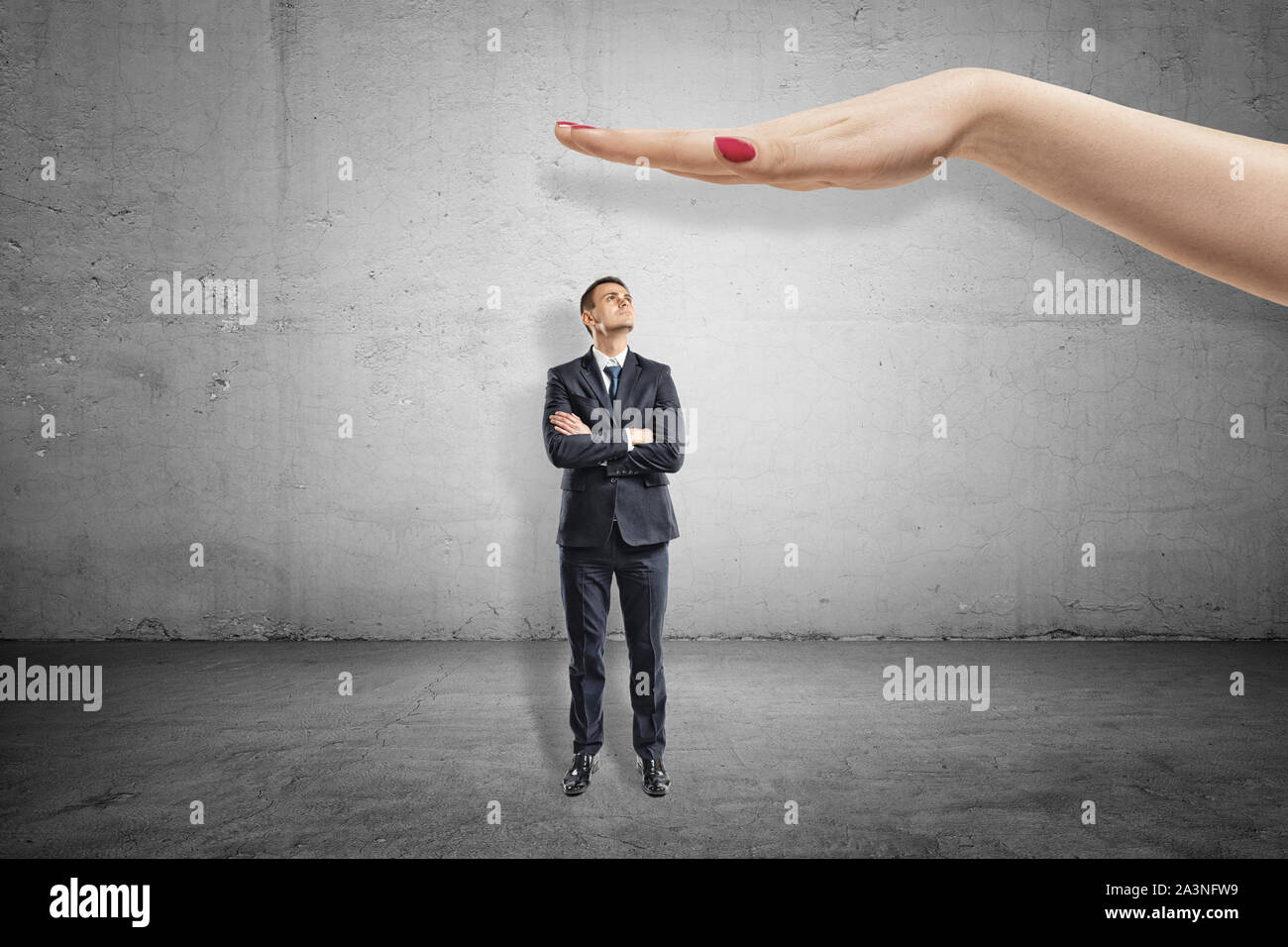 Big female hand over young serious businessman who is looking up on ...