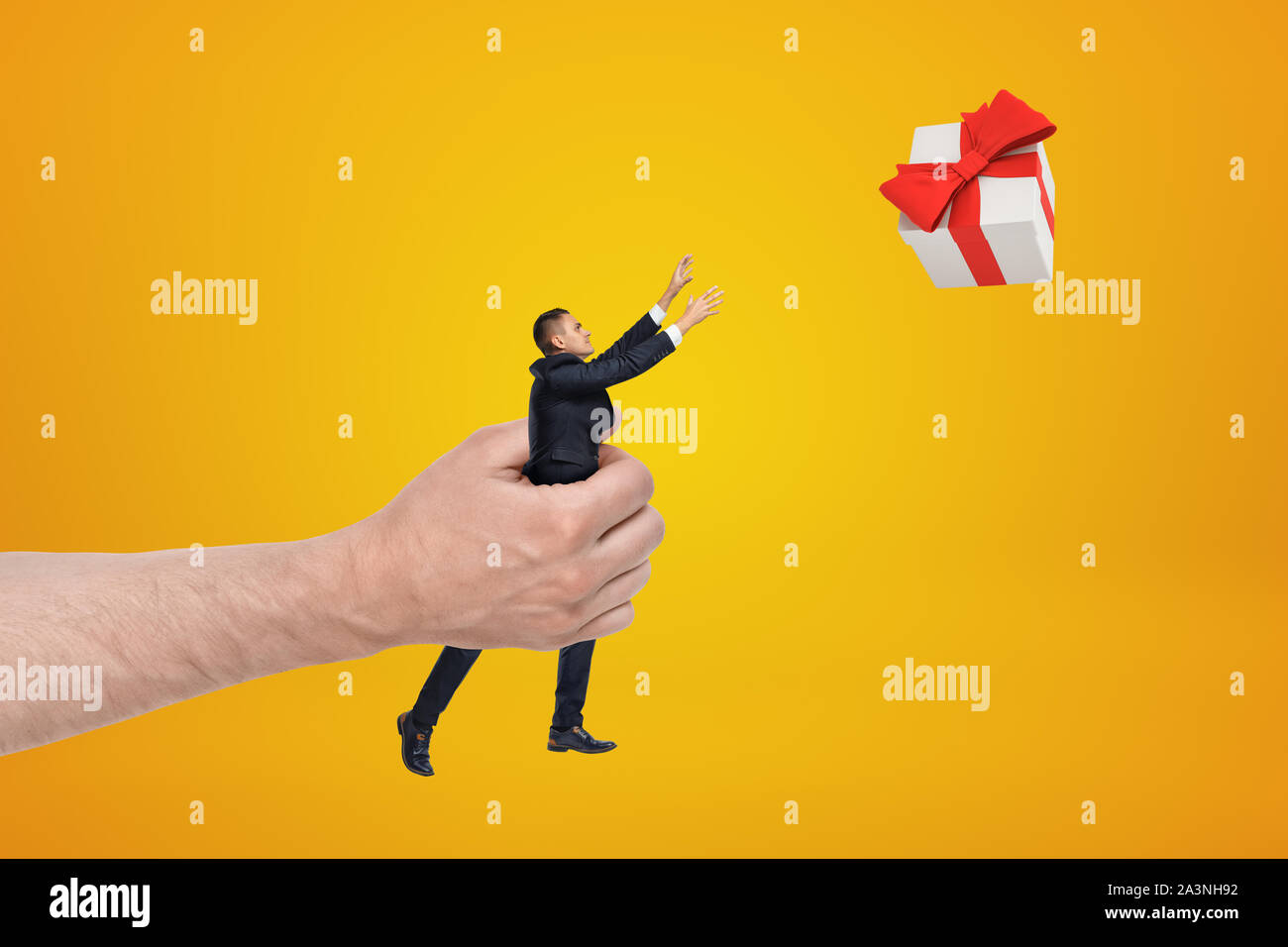 Big male hand holding businessman reaching out to gift box on yellow ...