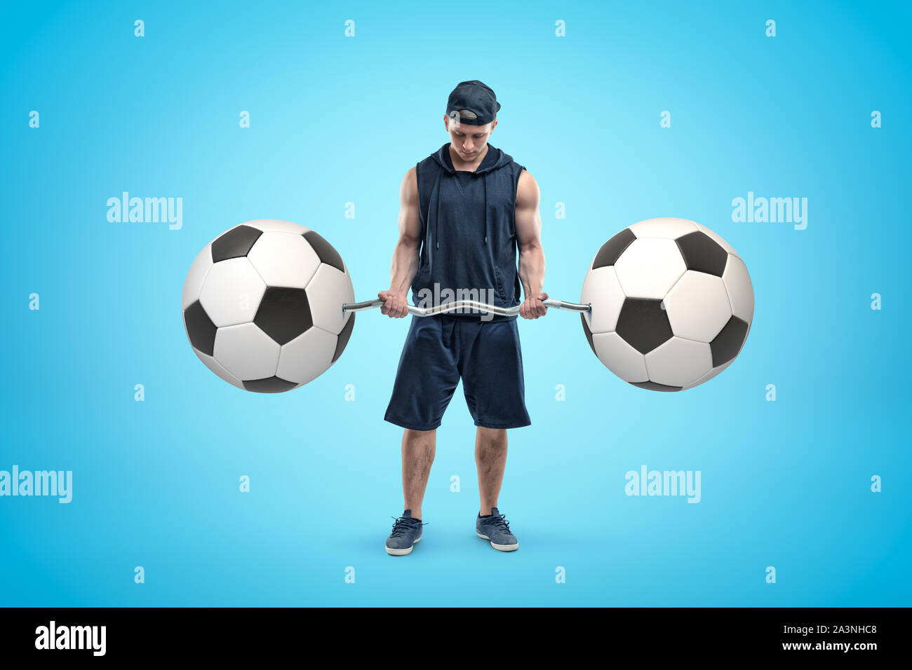 Strong muscular young man holding bar-bell with two football balls on ...