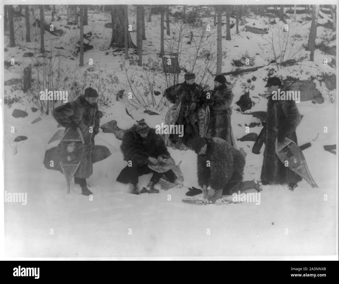 Six men in heavy fur coats putting on snowshoes Stock Photo - Alamy