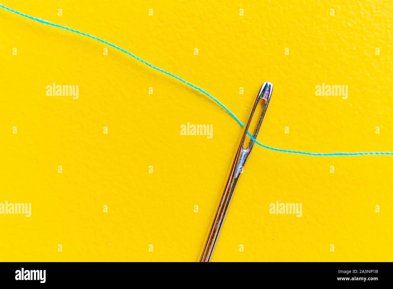 macro shot of a needle eye with a thread going through it on color ...