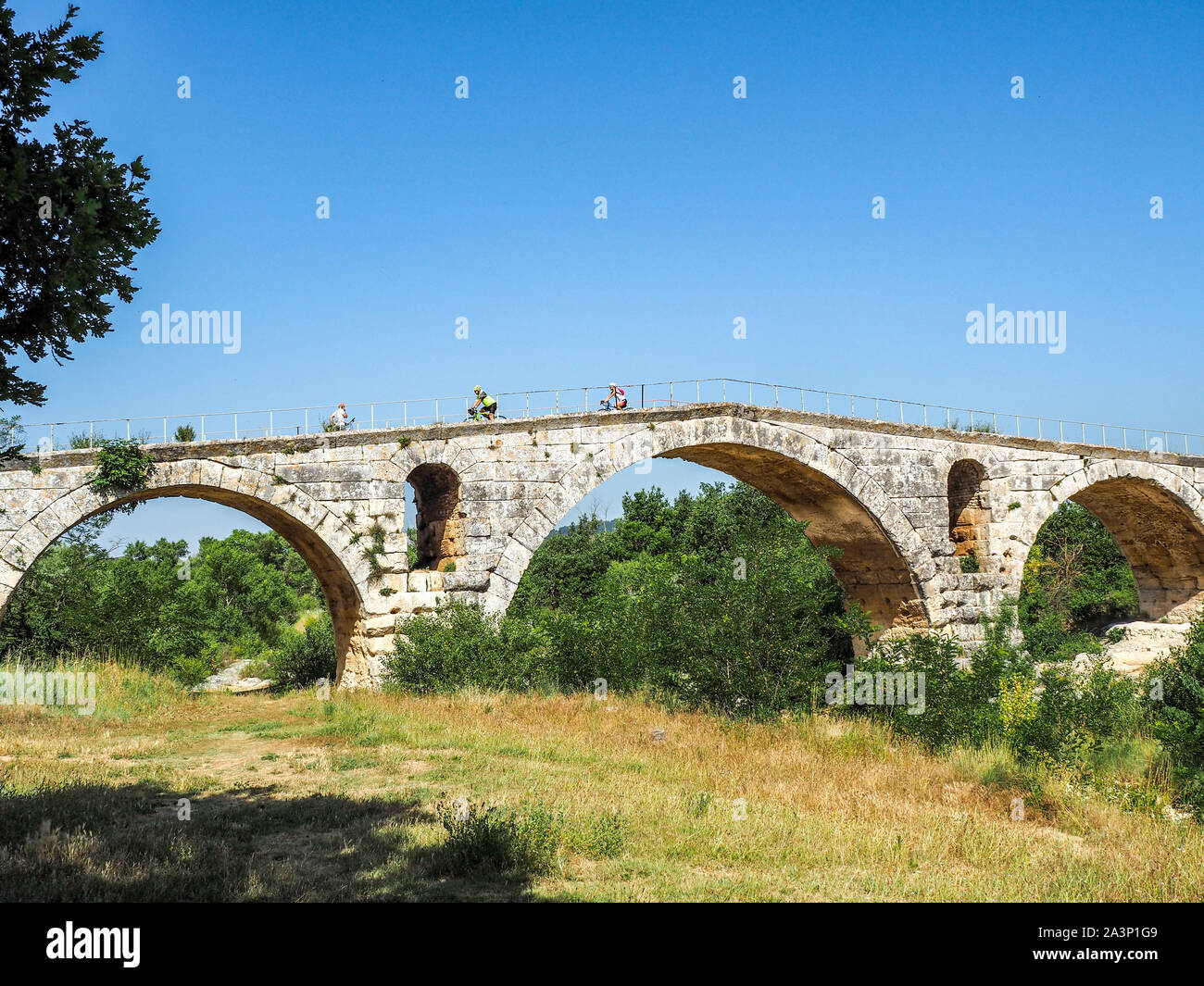 Bicyclists crossing old stone bridge while touring French countryside ...