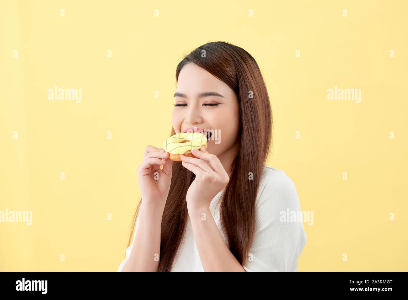 Portrait of a lovely young asian woman eating donuts isolated over ...