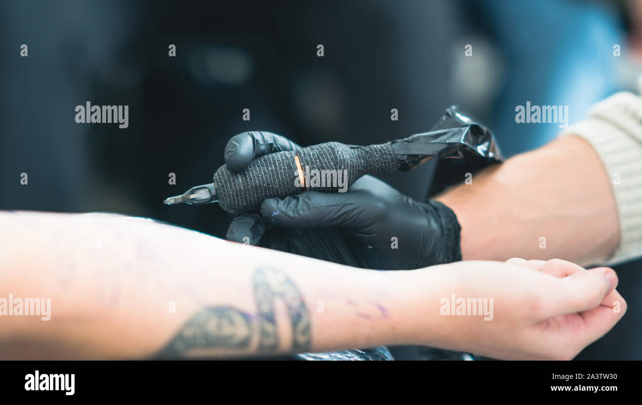Professional tattoo artist makes a tattoo on a young man’s hand, close ...