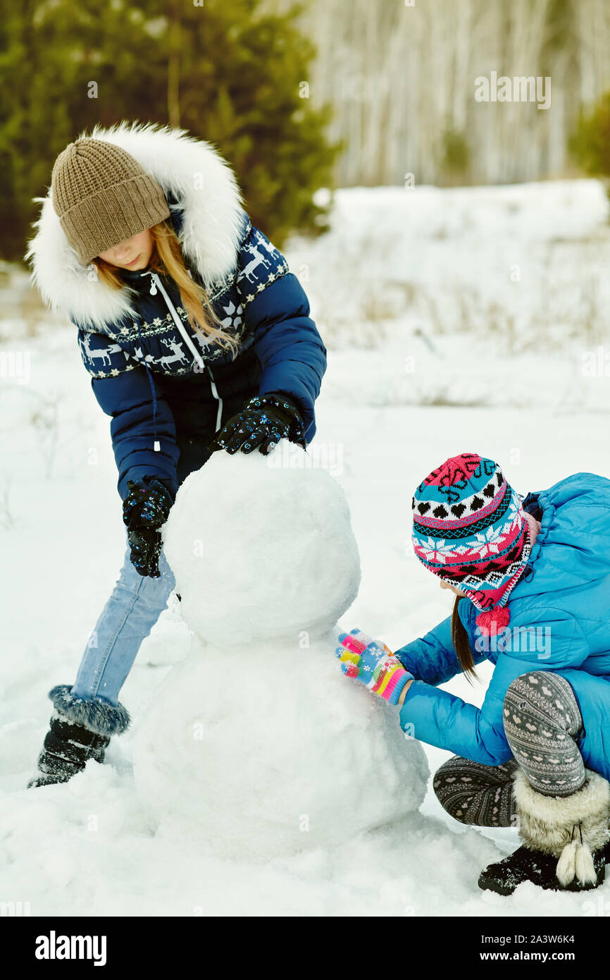 two female friends building a snowman. funny girls on a walk in the ...