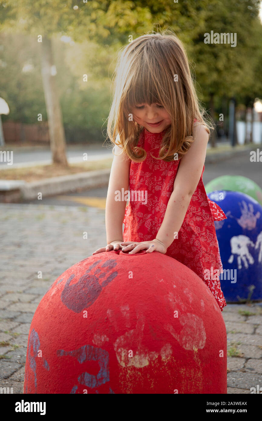 Little child girl playing with red concrete bollard at sunset in urban ...