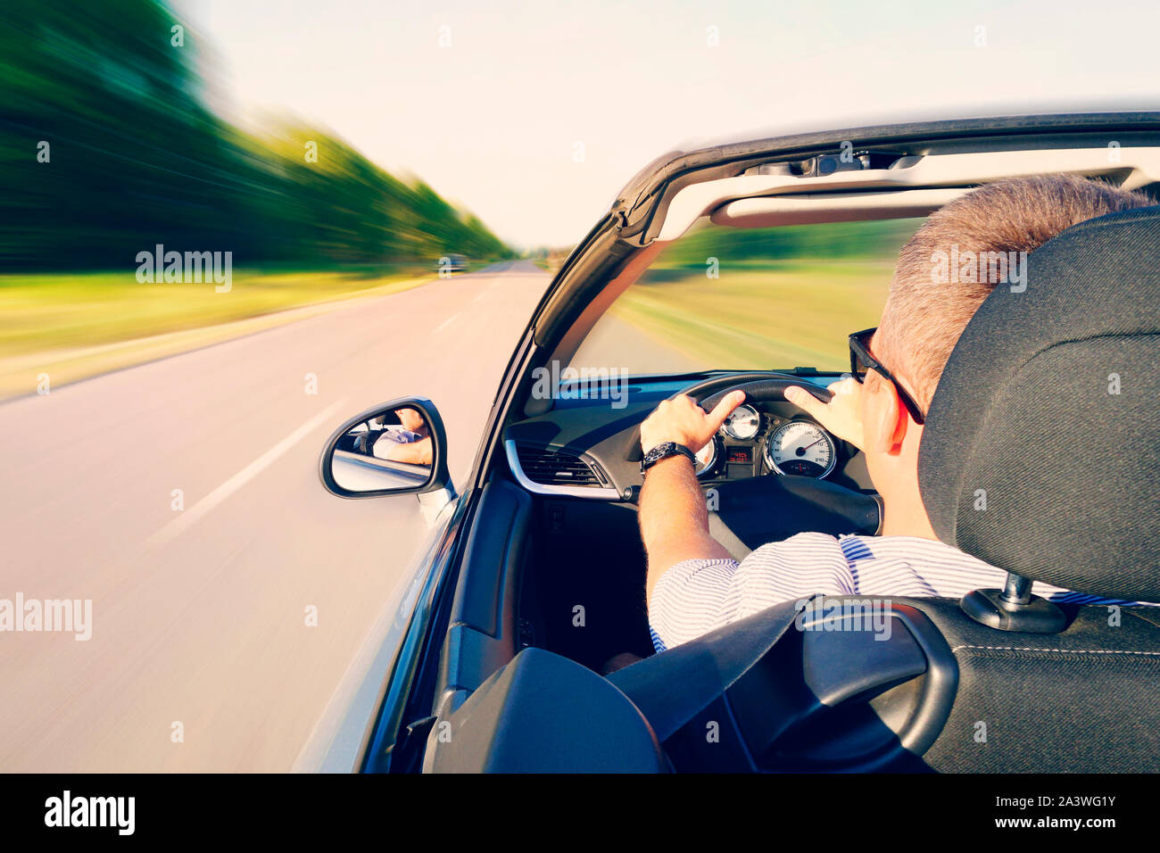 Man driving a convertible car on country road. View from the inside ...