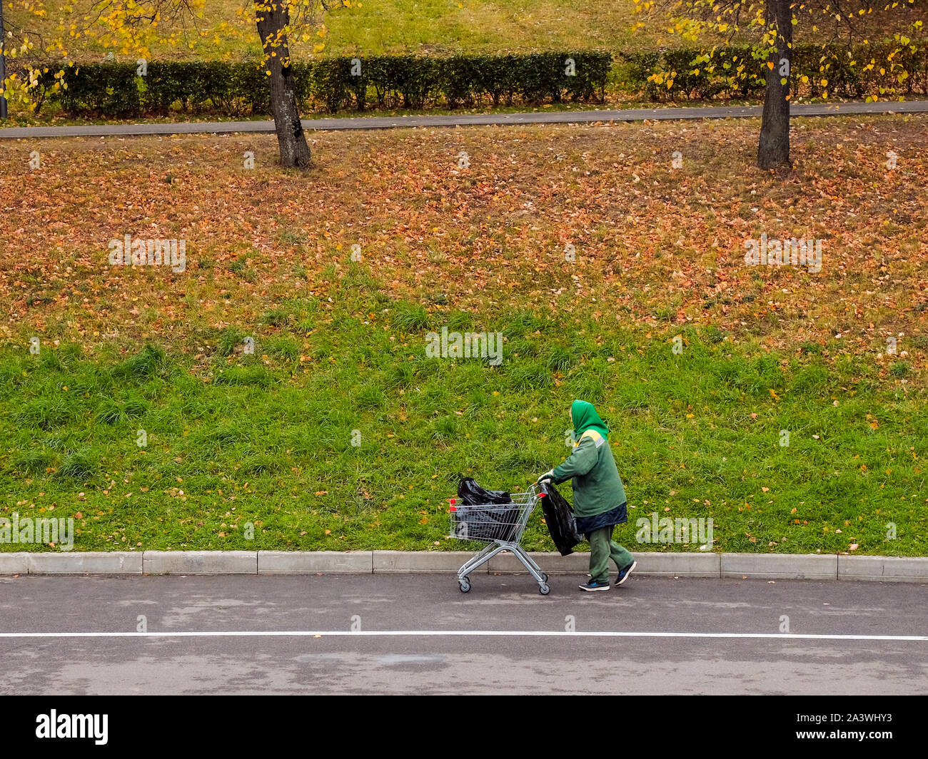 A woman in green overalls carries plastic bags in a shopping cart ...