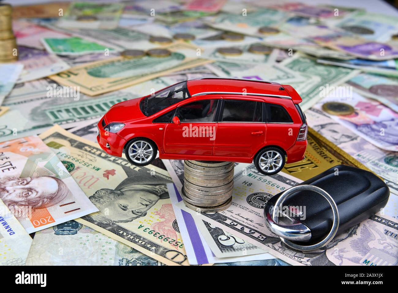 A car key and a red toy car on a tower made of coins. Background of ...