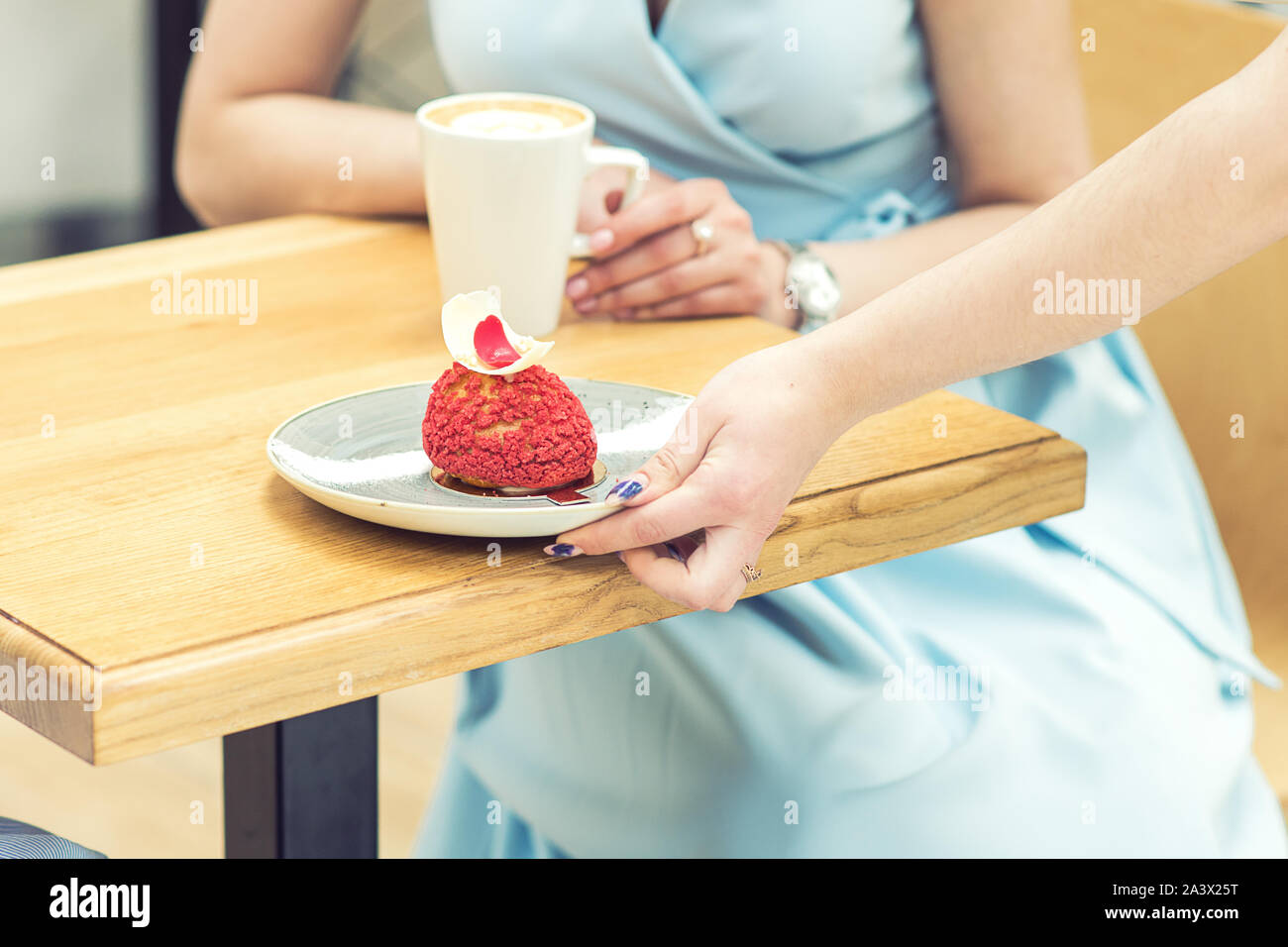 The hand of the waiter puts the piece of cake on the table while female ...