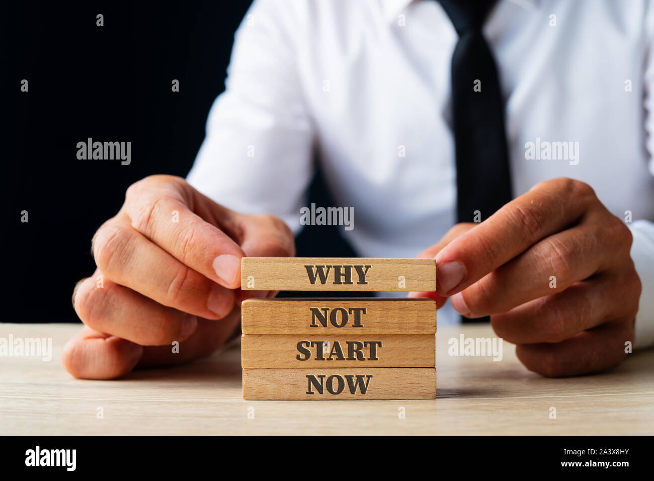 Businessman stacking wooden pegs to assemble the Why not start now sign ...