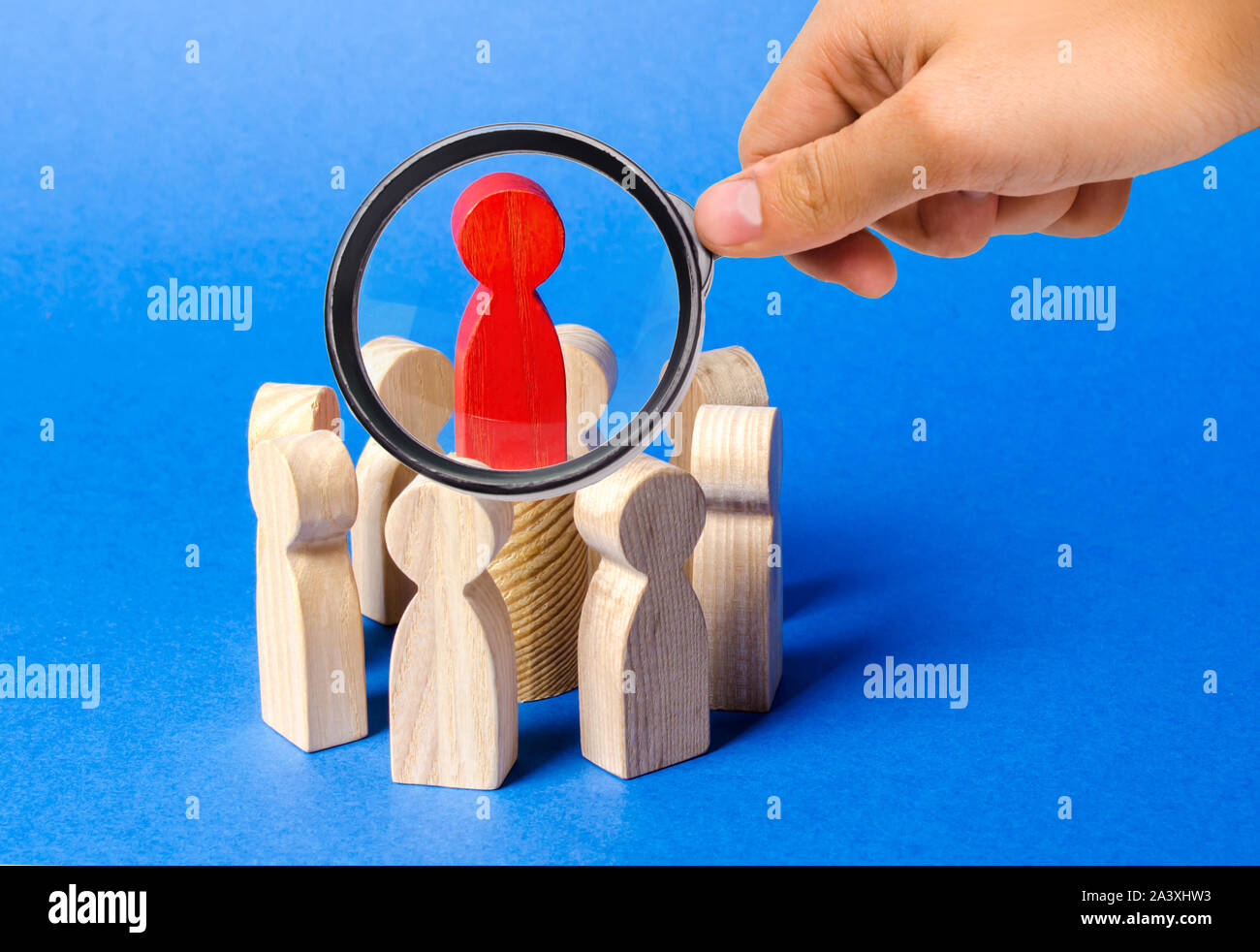 A magnifying glass looks at a red figure of the leader in the center of ...