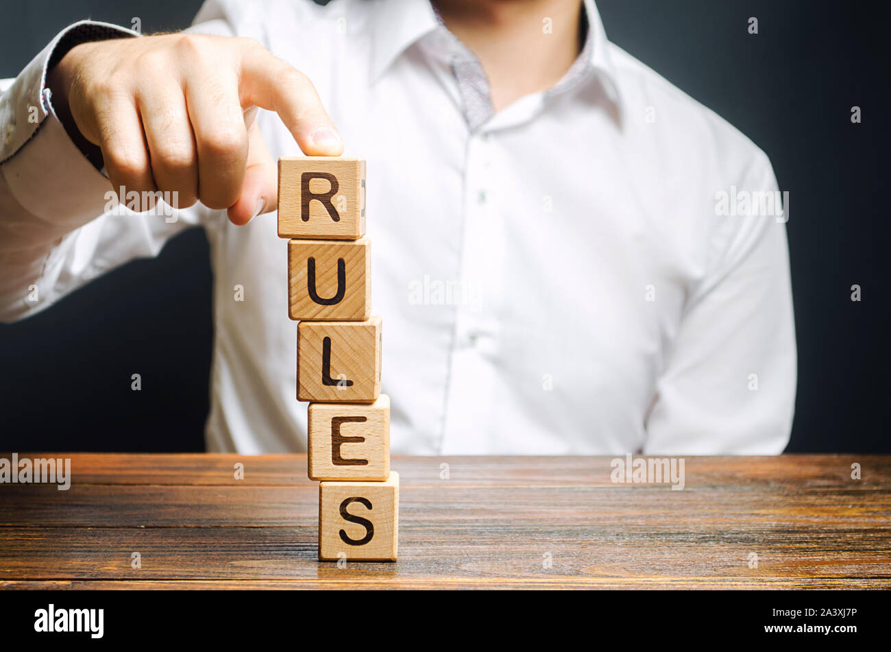 A man holds a tower of blocks with the word Rules from falling. Setting ...