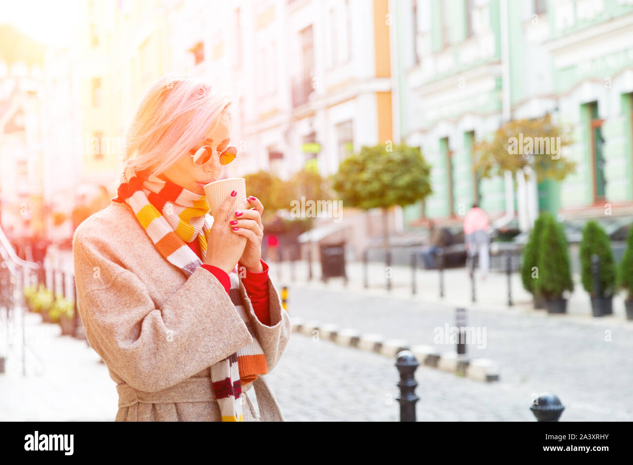 A young girl walks around the old city and drinks a warm drink. Autumn ...