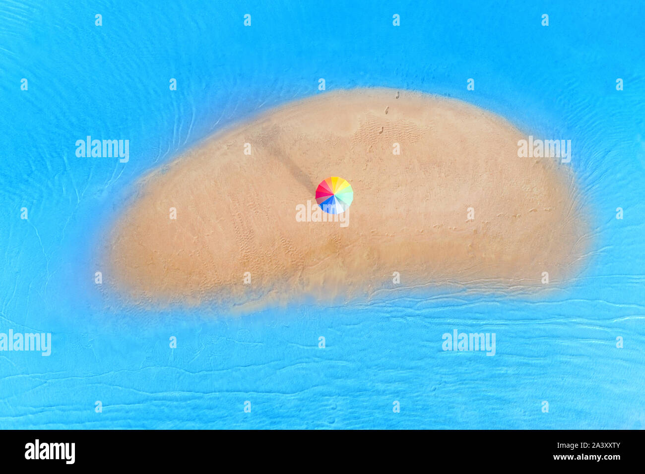 Small sandy island with someone under rainbow colored umbrella on it ...