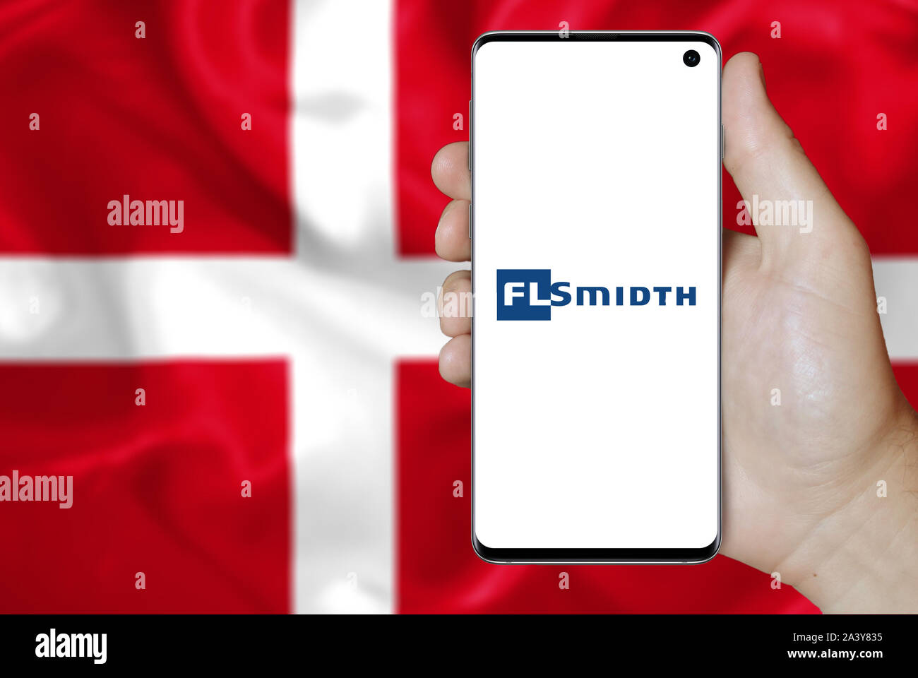 A man holds a phone displaying the logo of company FLSmidth & Co ...