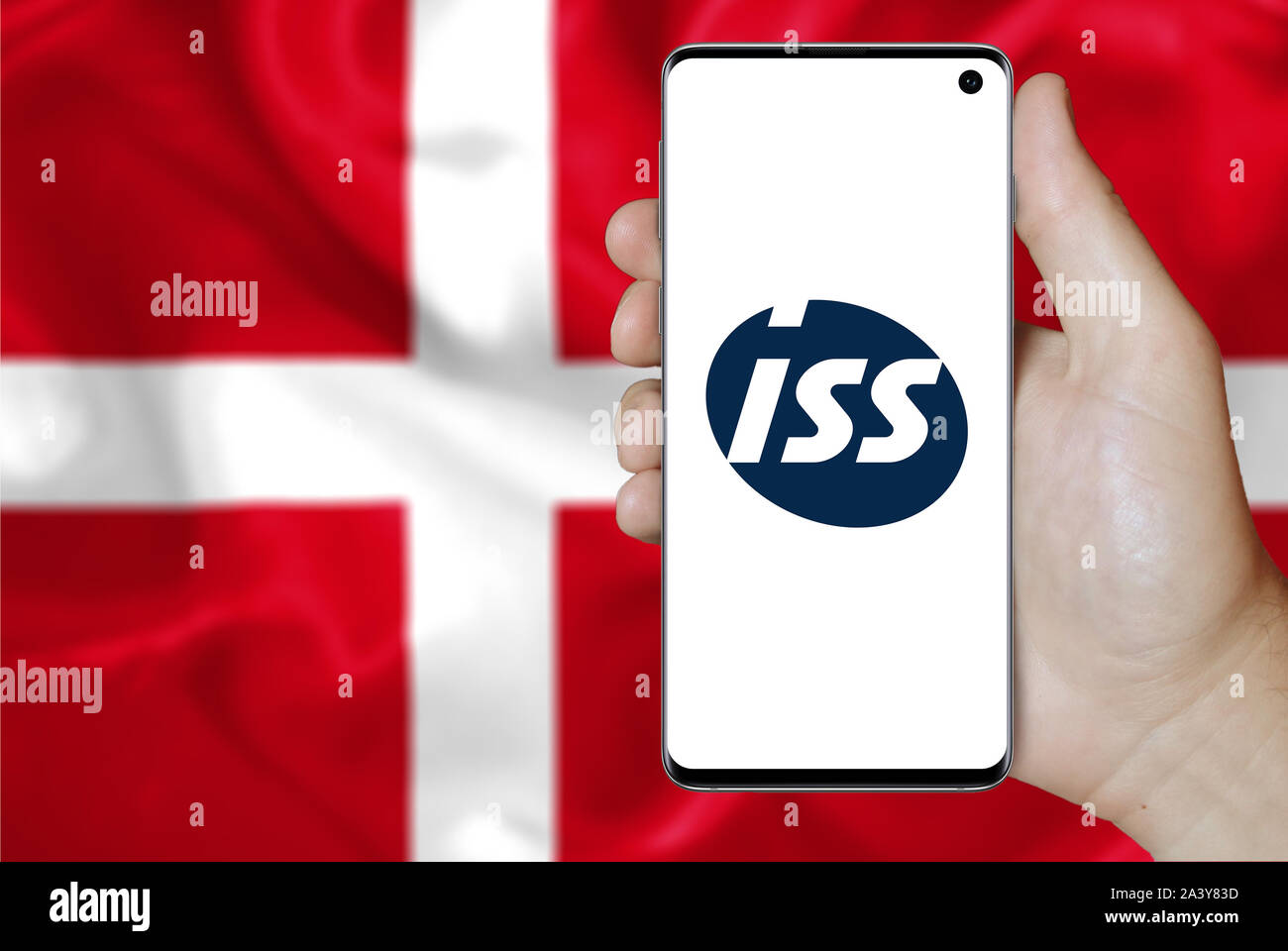 A man holds a phone displaying the logo of company ISS listed on OMX Copenhagen. Danish flag ...