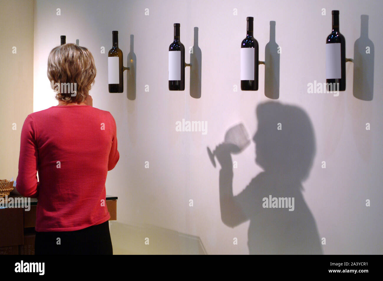 A standing woman drinking a glass of wine throwing her own shadow on ...