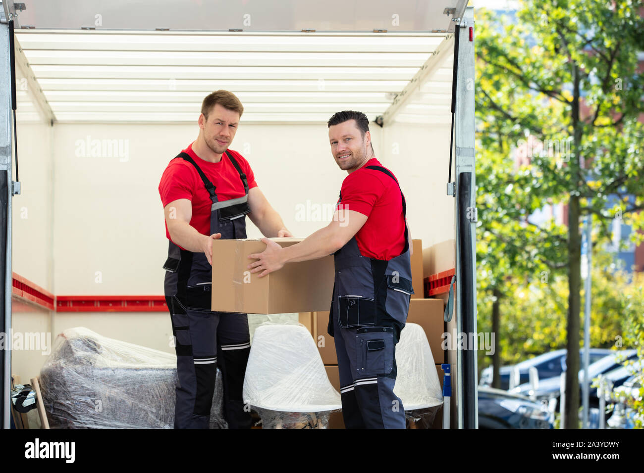 Two Young Men Unloading And Stacking The Brown Cardboard Boxes On Moving Truck Stock Photo - Alamy