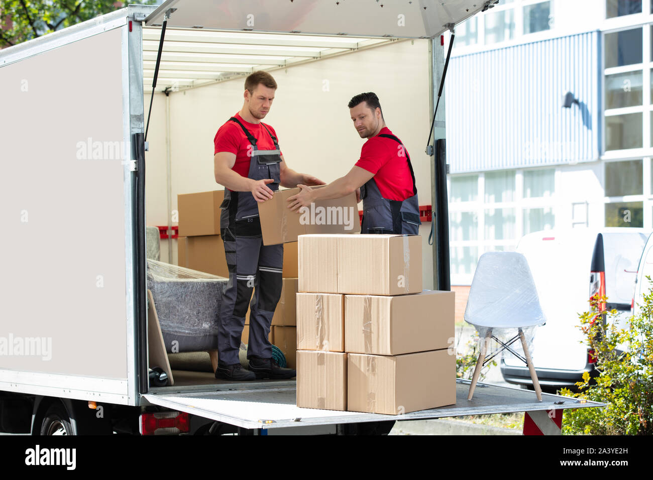 Two Young Men Unloading And Stacking The Brown Cardboard Boxes On ...